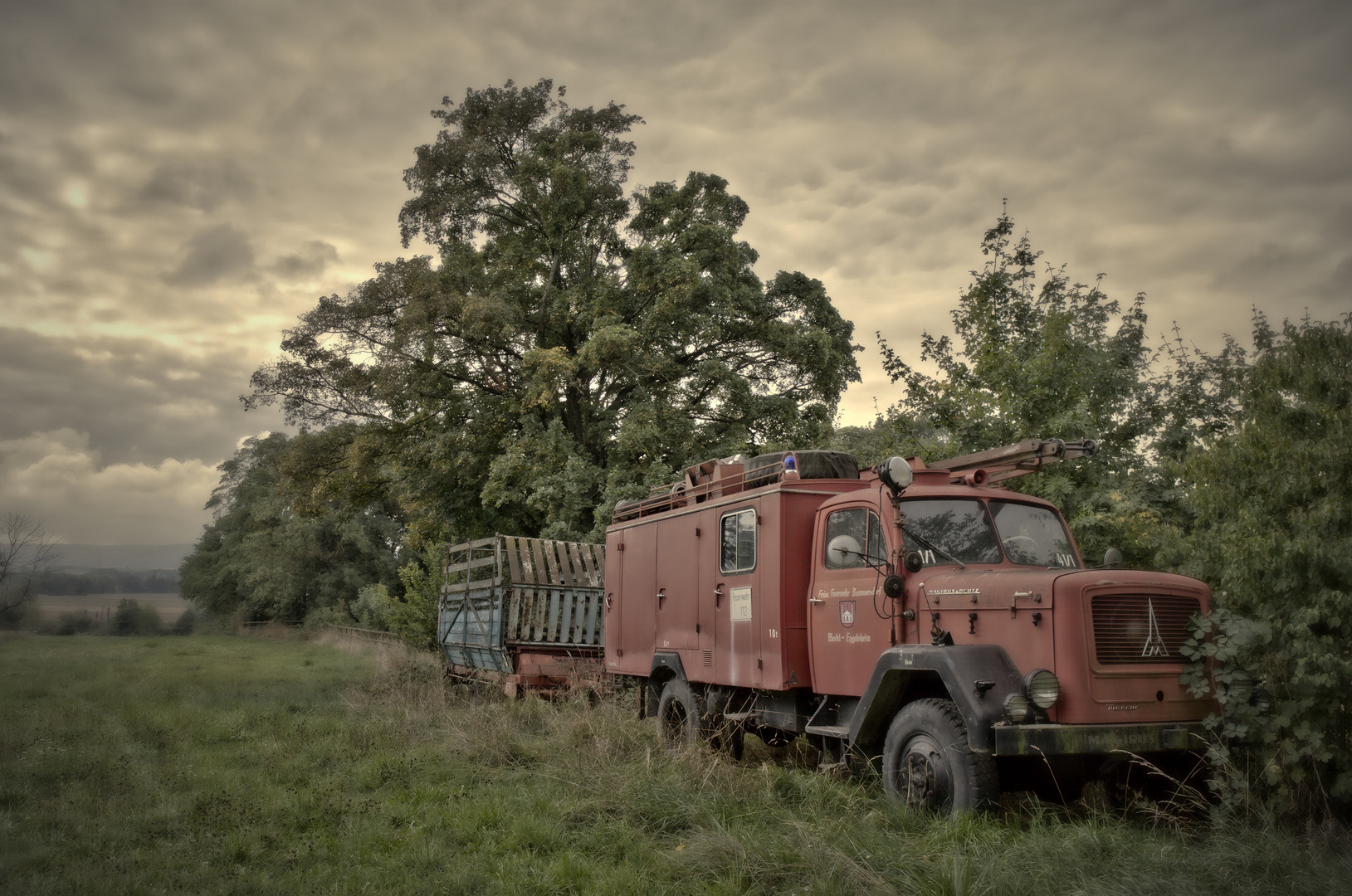 ein seltsames Gespann - altes Feuerwehrauto und Ladewagen auf grüner ...